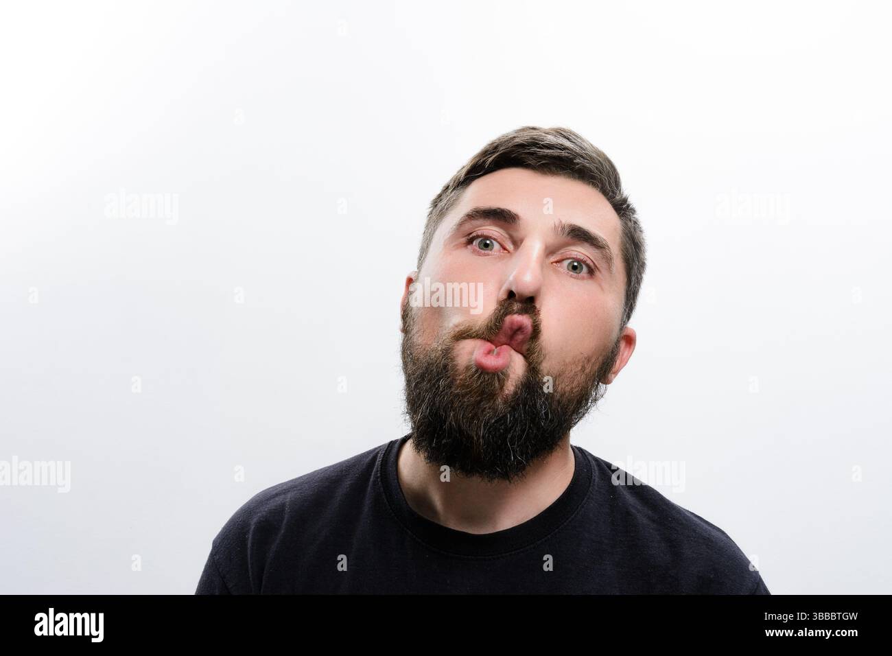 A man with a beard pulls a humorous face against a plain white backdrop ...