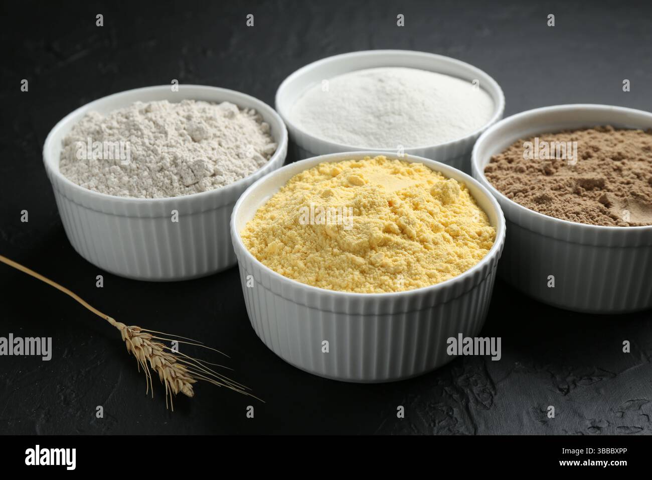 Different types of flour in bowls and spike on black textured table ...
