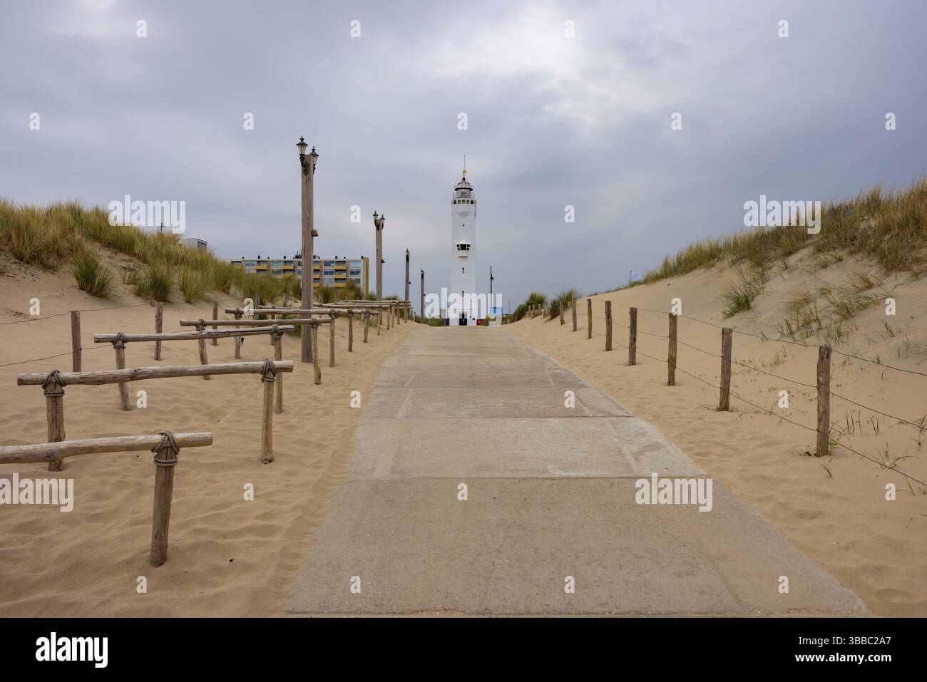 Concrete path leading to white lighthouse with sand dunes and wooden ...