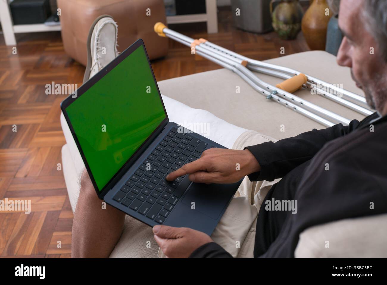 Man with broken leg and crutches is working from home using laptop with ...