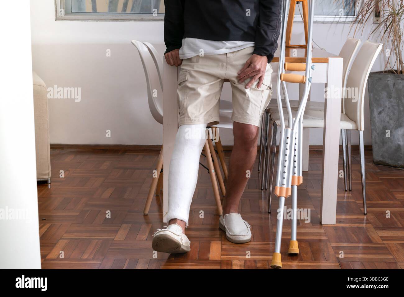 Man with broken leg plaster using crutches at home leaning on table ...