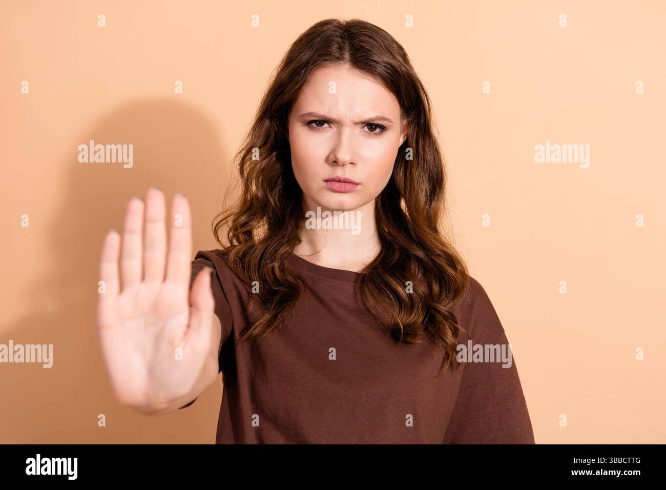Serious young woman showcases a stop hand gesture on a beige background ...