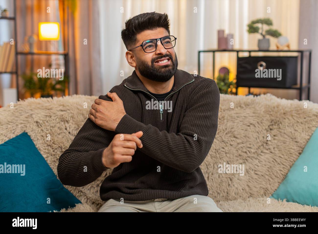 Indian man at home holds shoulder with tension, showing pain on his ...