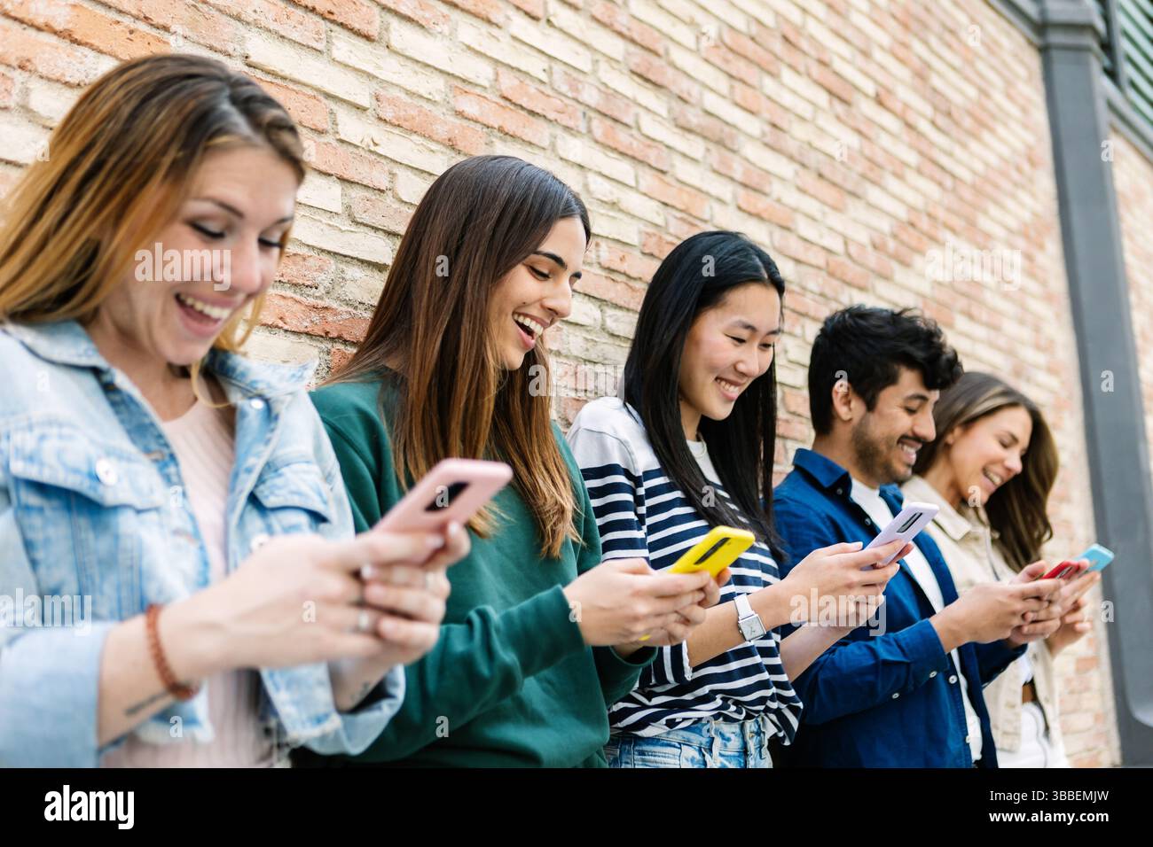 Young people using mobile phones and smiling by brick wall Stock Photo ...