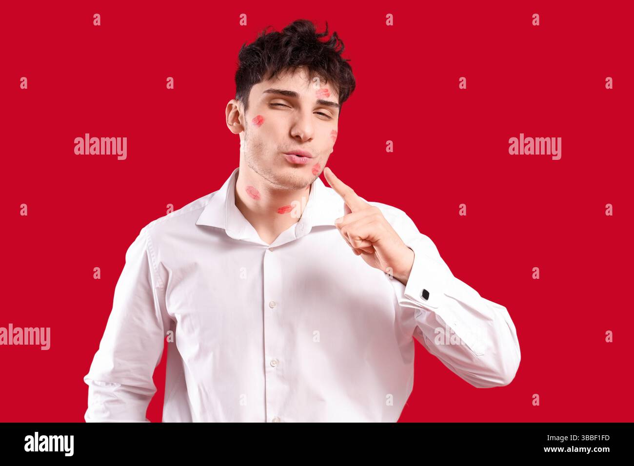 Handsome young man with lips marks on his face blowing kiss against red ...