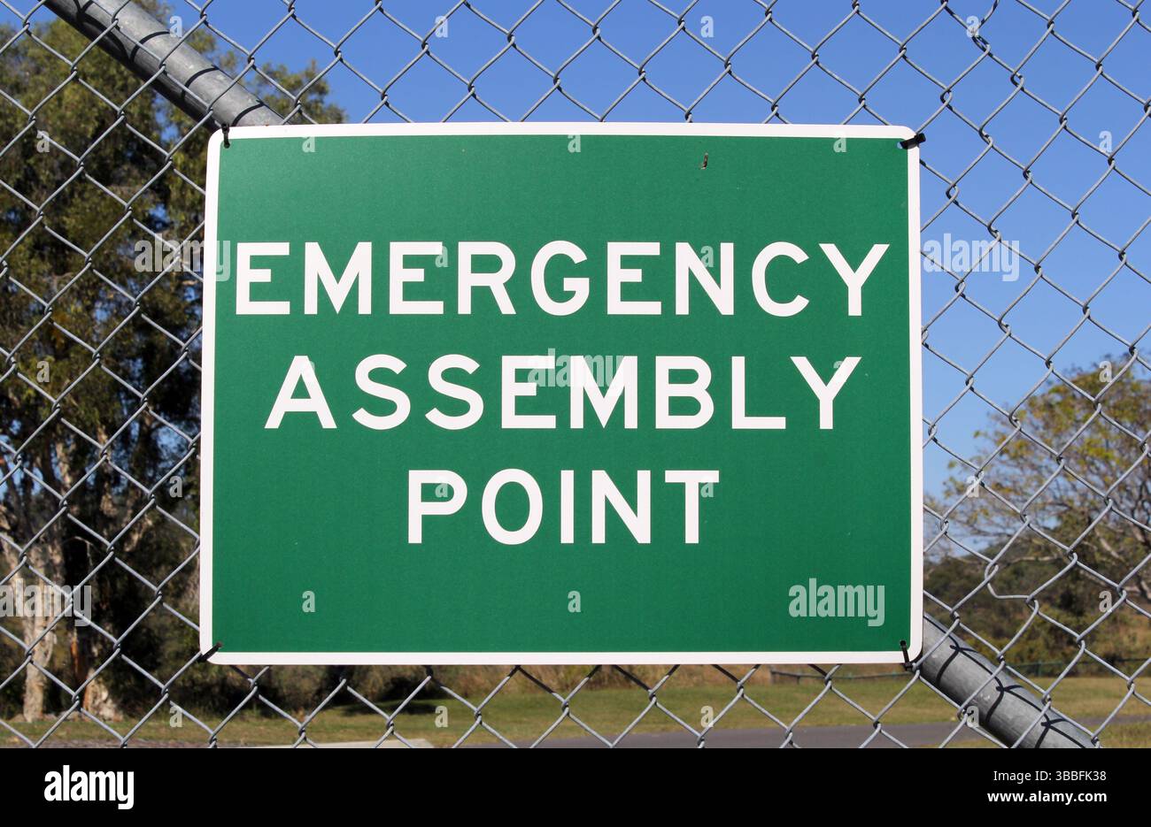 Green Emergency Assembly Point sign attached to a chain-link fence ...