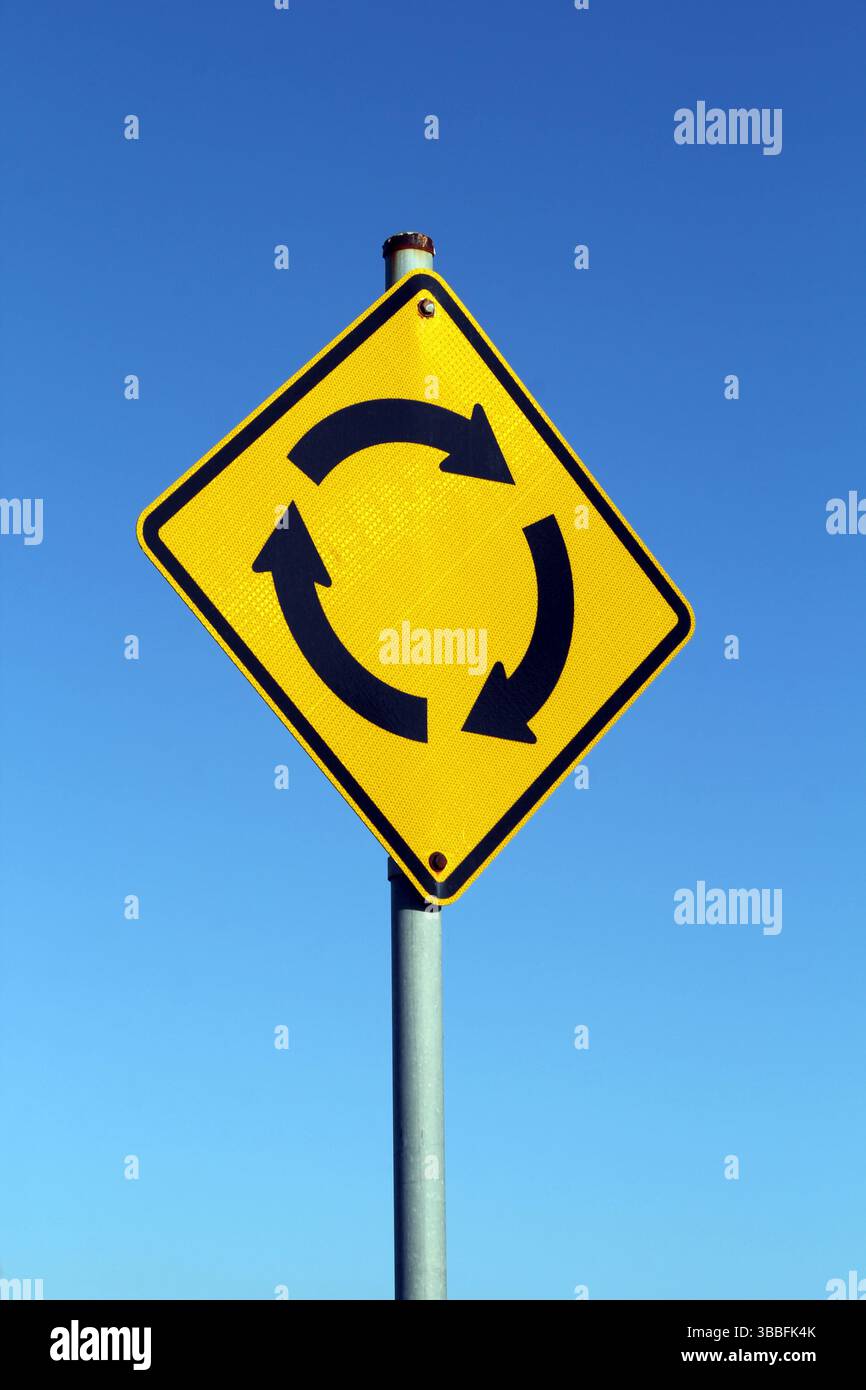 Yellow roundabout traffic circle sign against a clear blue sky ...