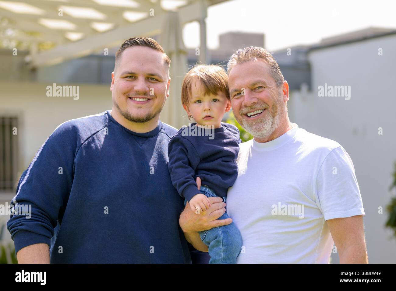 Three generations of one family stand together in a sunlit garden ...