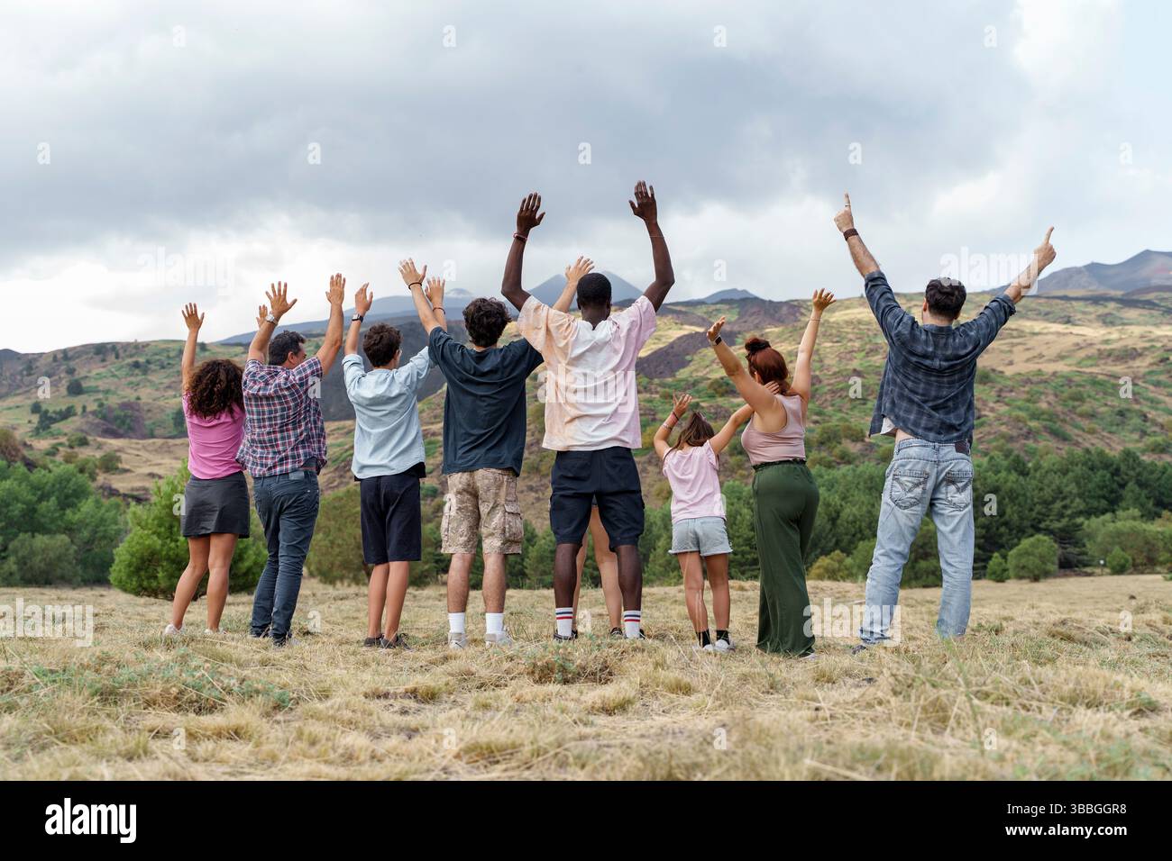 Back view of a diverse group of friends raising hands in the air while ...