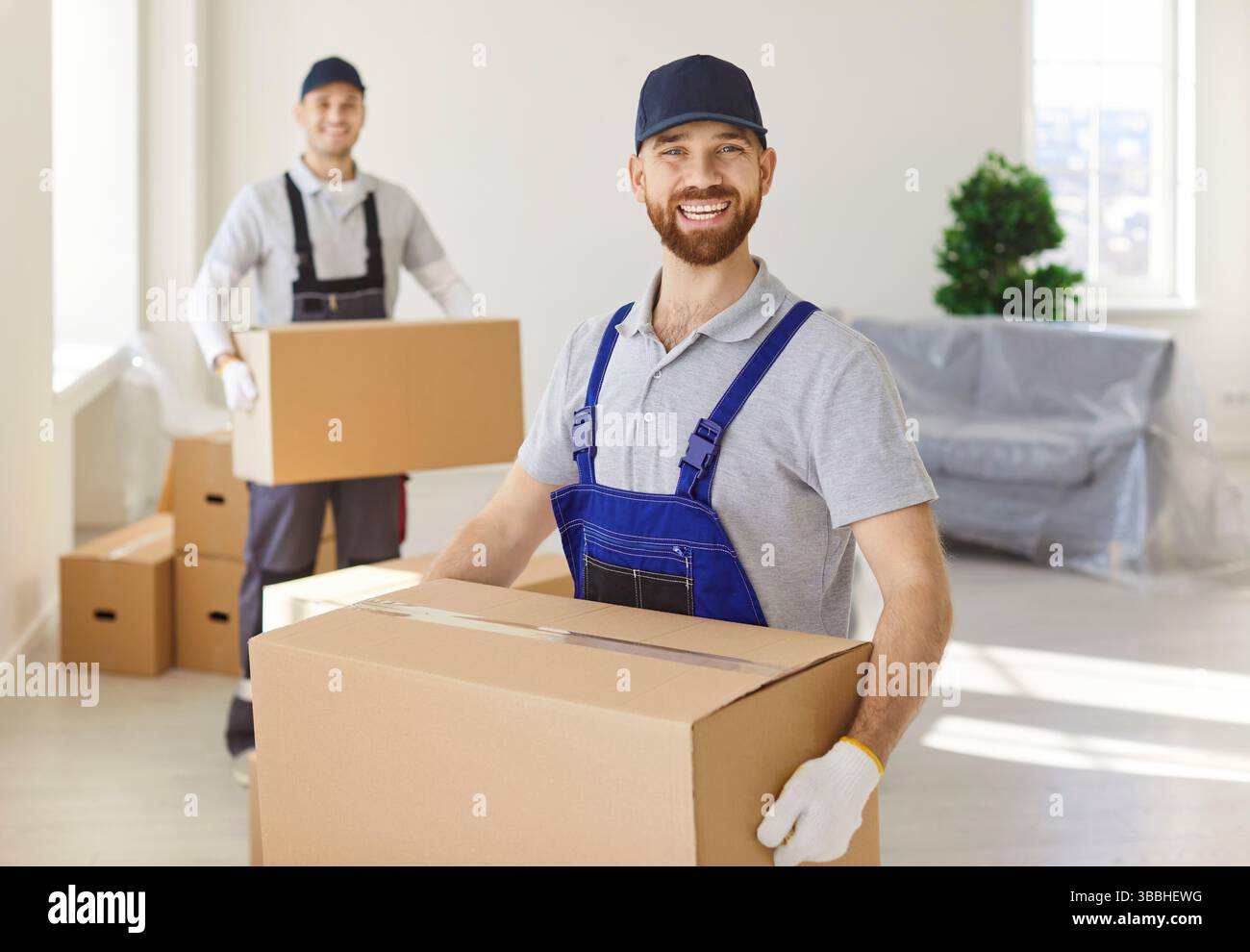 Happy men workers from removal service carrying packed cardboard boxes ...