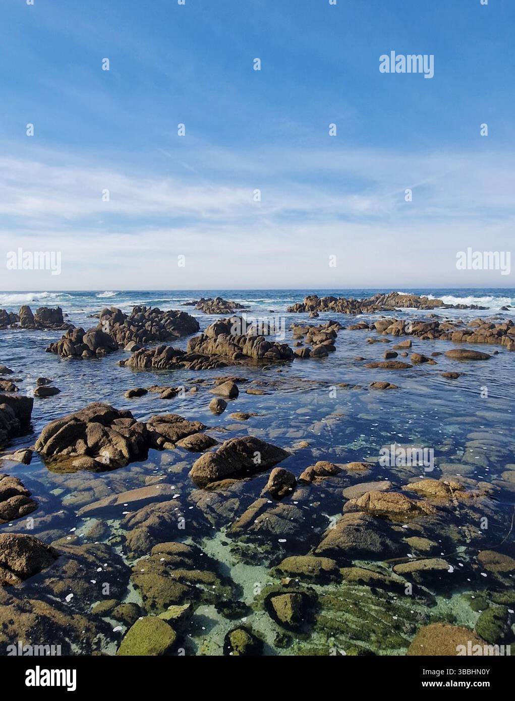 Rocky shoreline under a clear sky with calm waves Stock Photo - Alamy