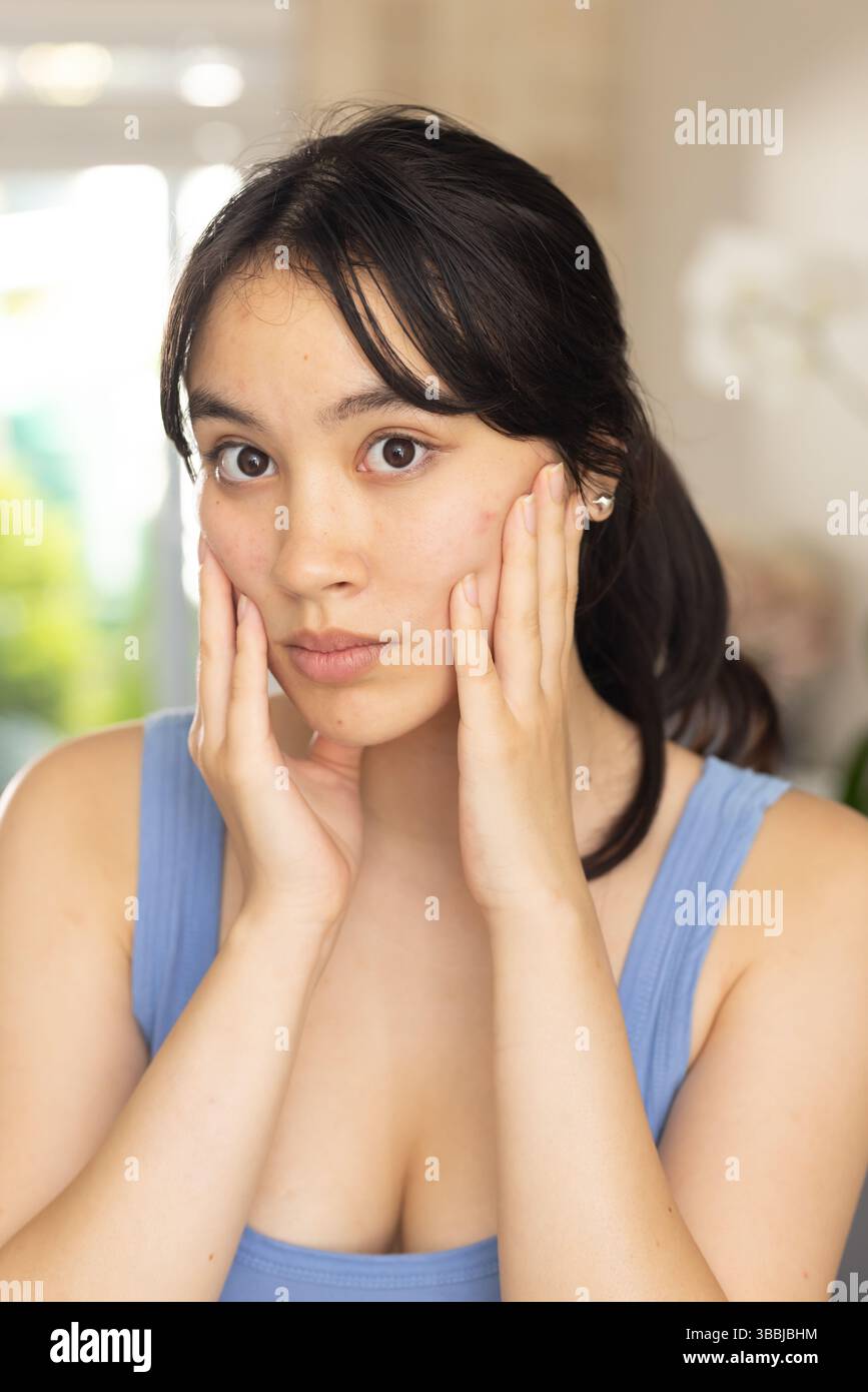 Gently pressing cheeks Asian woman standing near window at home, with soft natural light Stock ...