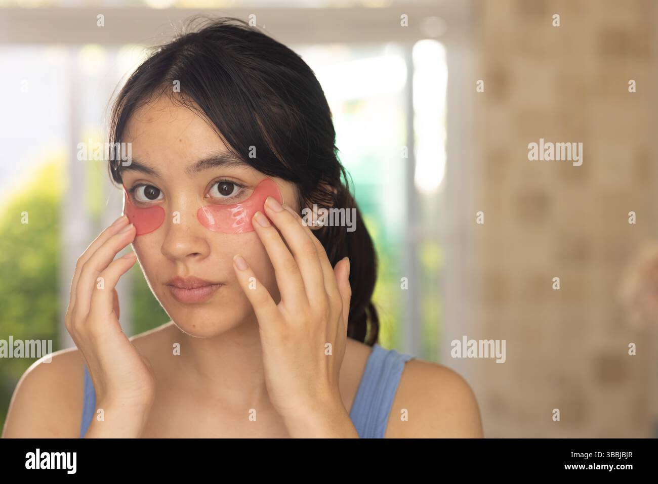 Placing pink hydrogel eye patches under eyes, Asian woman at home near ...