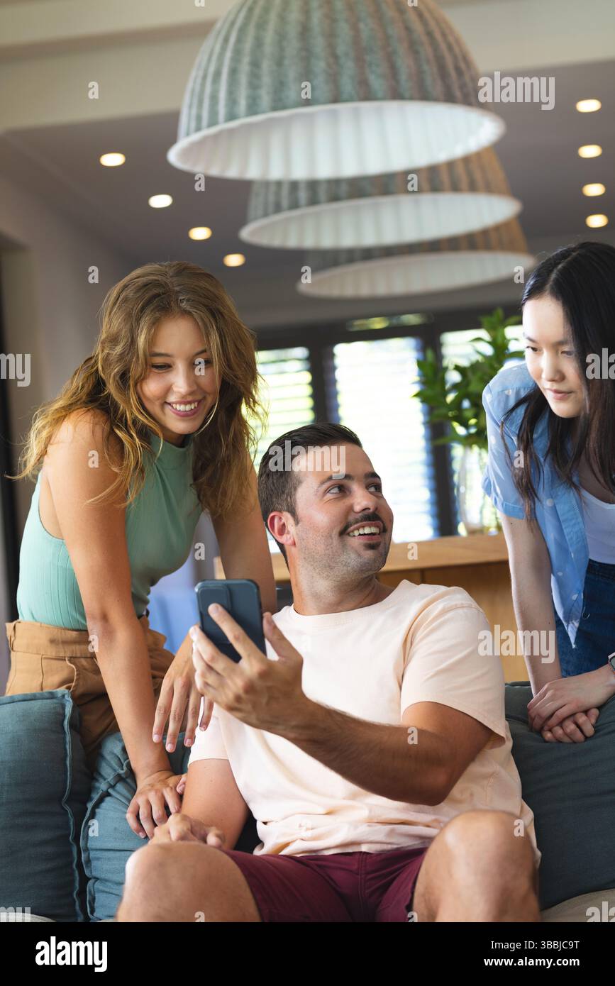 Viewing smartphone screen, diverse friends leaning on sofa in living ...
