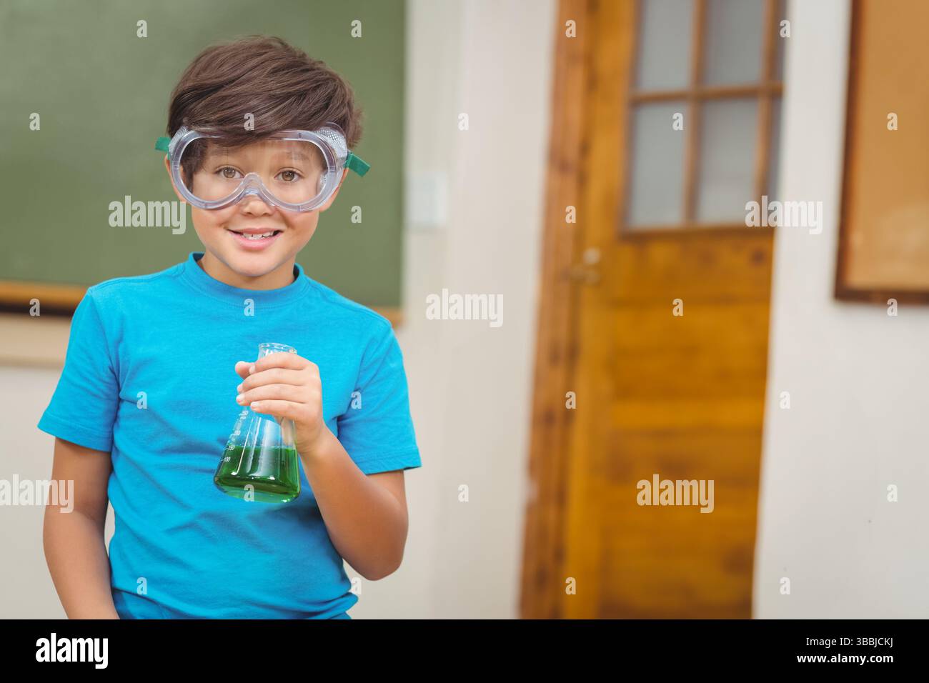 Boy wearing goggles holding Erlenmeyer flask containing green liquid in ...