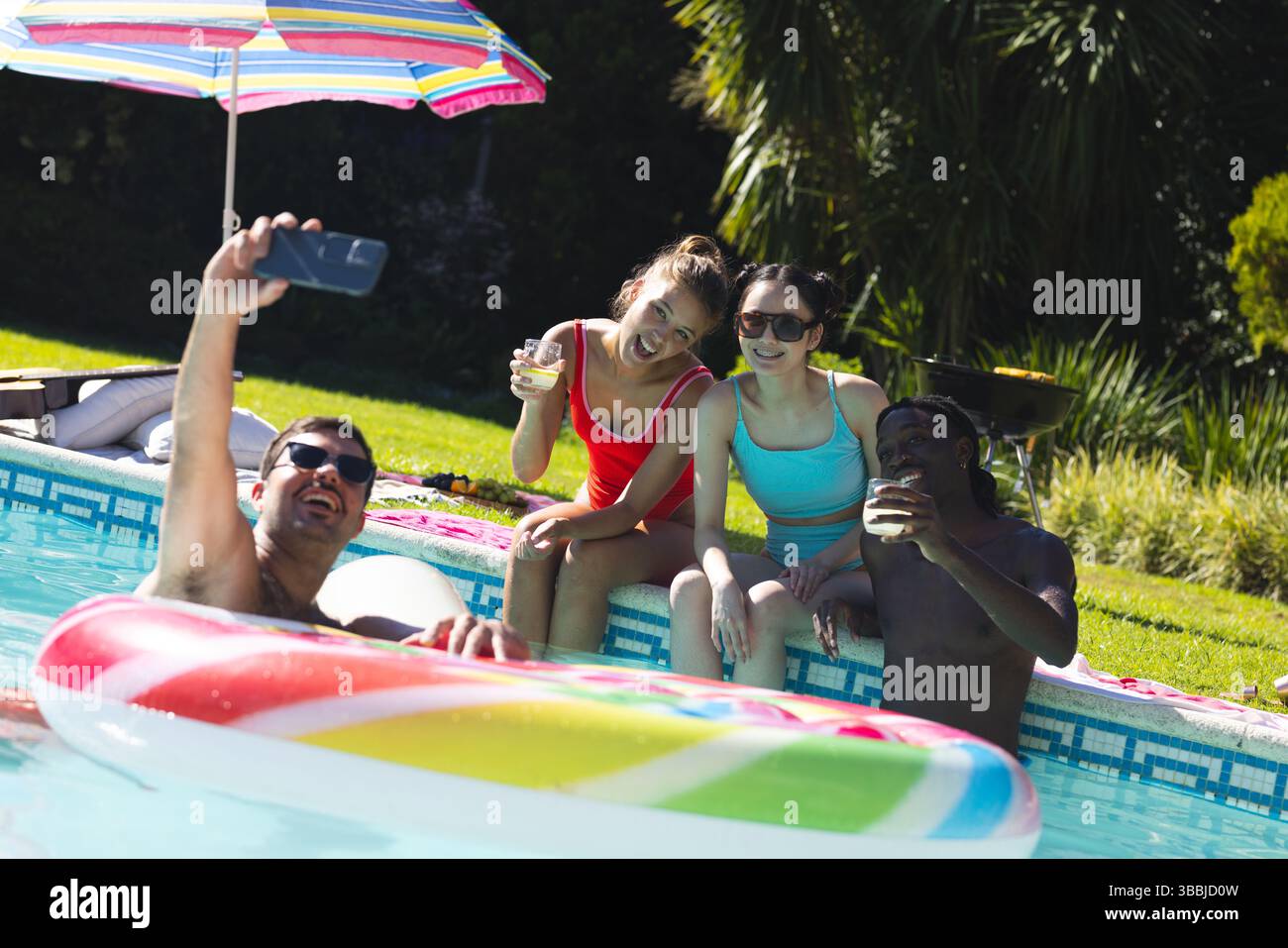 Relaxing Diverse friends lounging on pool float under striped umbrella ...