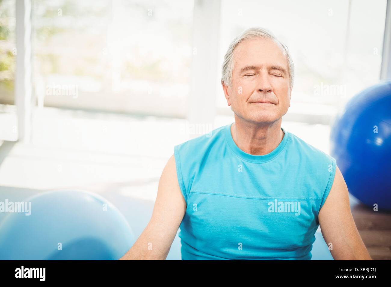 Meditating Senior man sitting cross-legged on floor in fitness studio ...