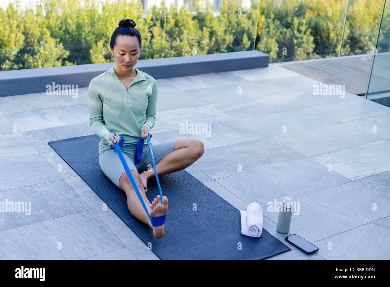 Stretching Asian woman pulling resistance band on rooftop, with towel ...