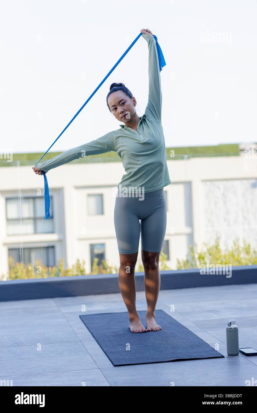 Standing Chinese woman stretching resistance band overhead on rooftop ...