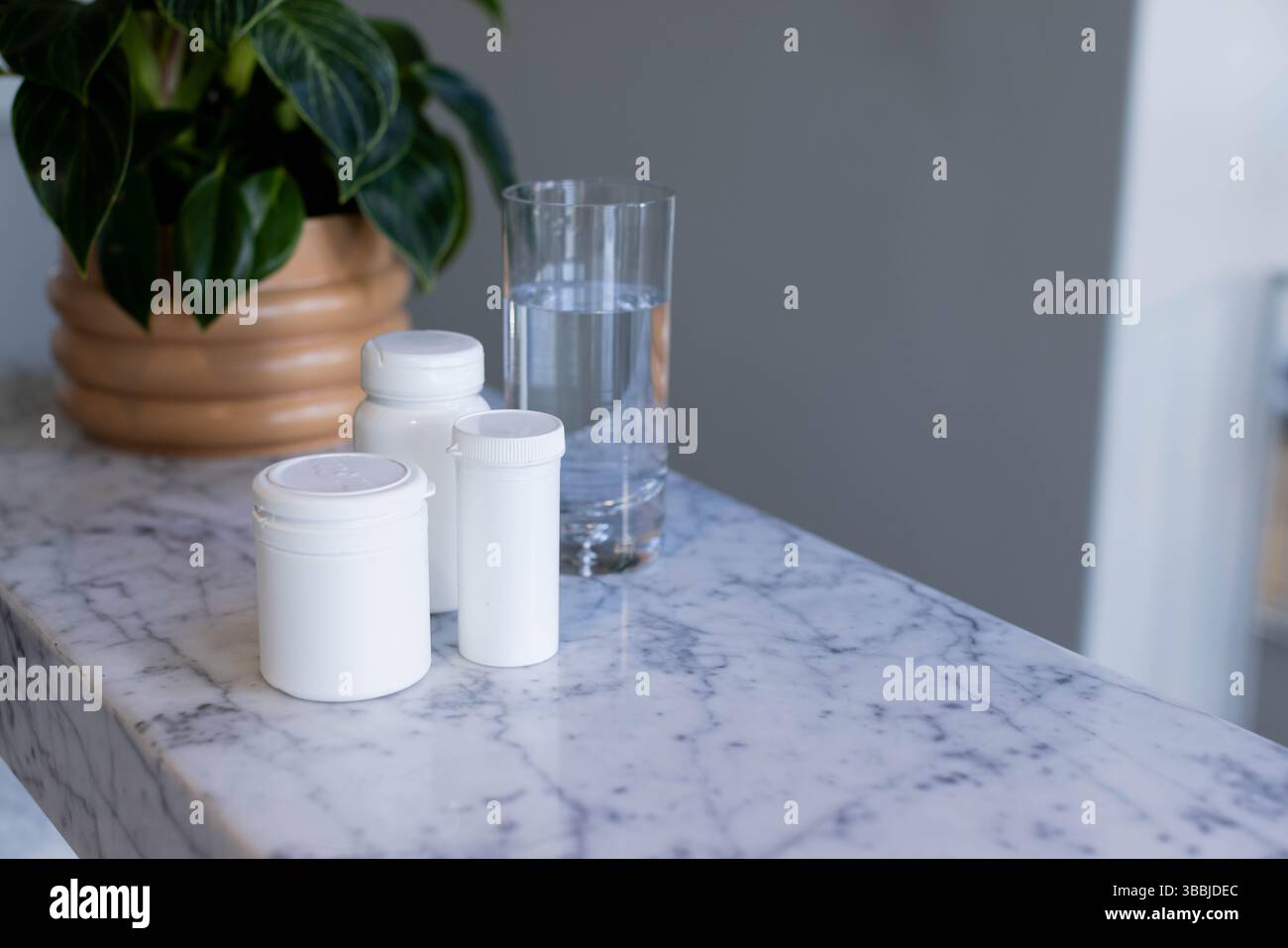 Three white medicine bottles are standing beside water glass on marble ...