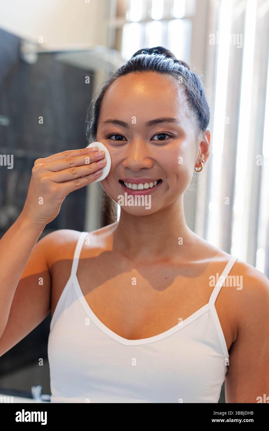 Holding cotton pad against cheek, Asian woman standing by bathroom sink ...
