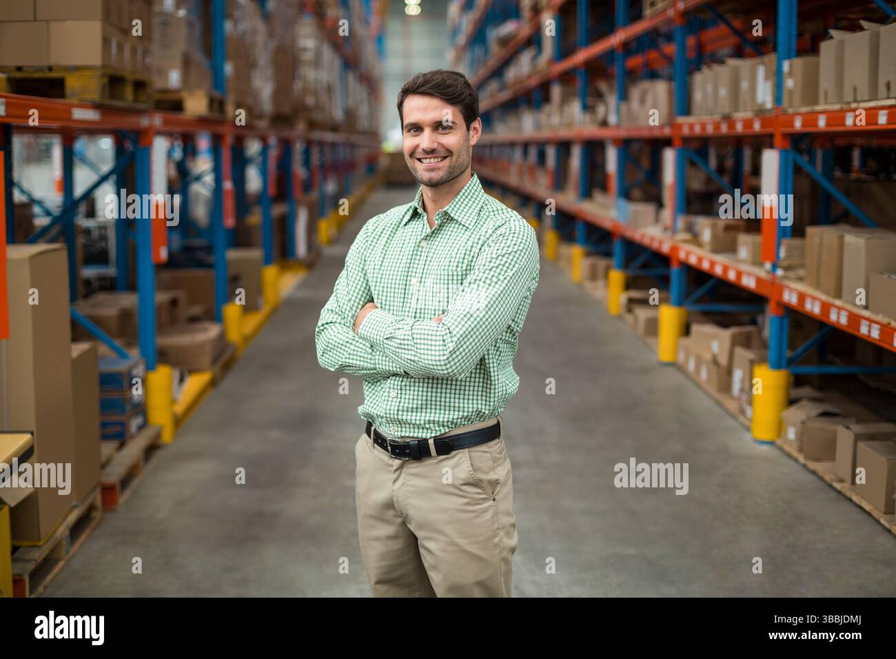 Standing man crossing arms in warehouse aisle, with cardboard boxes and ...