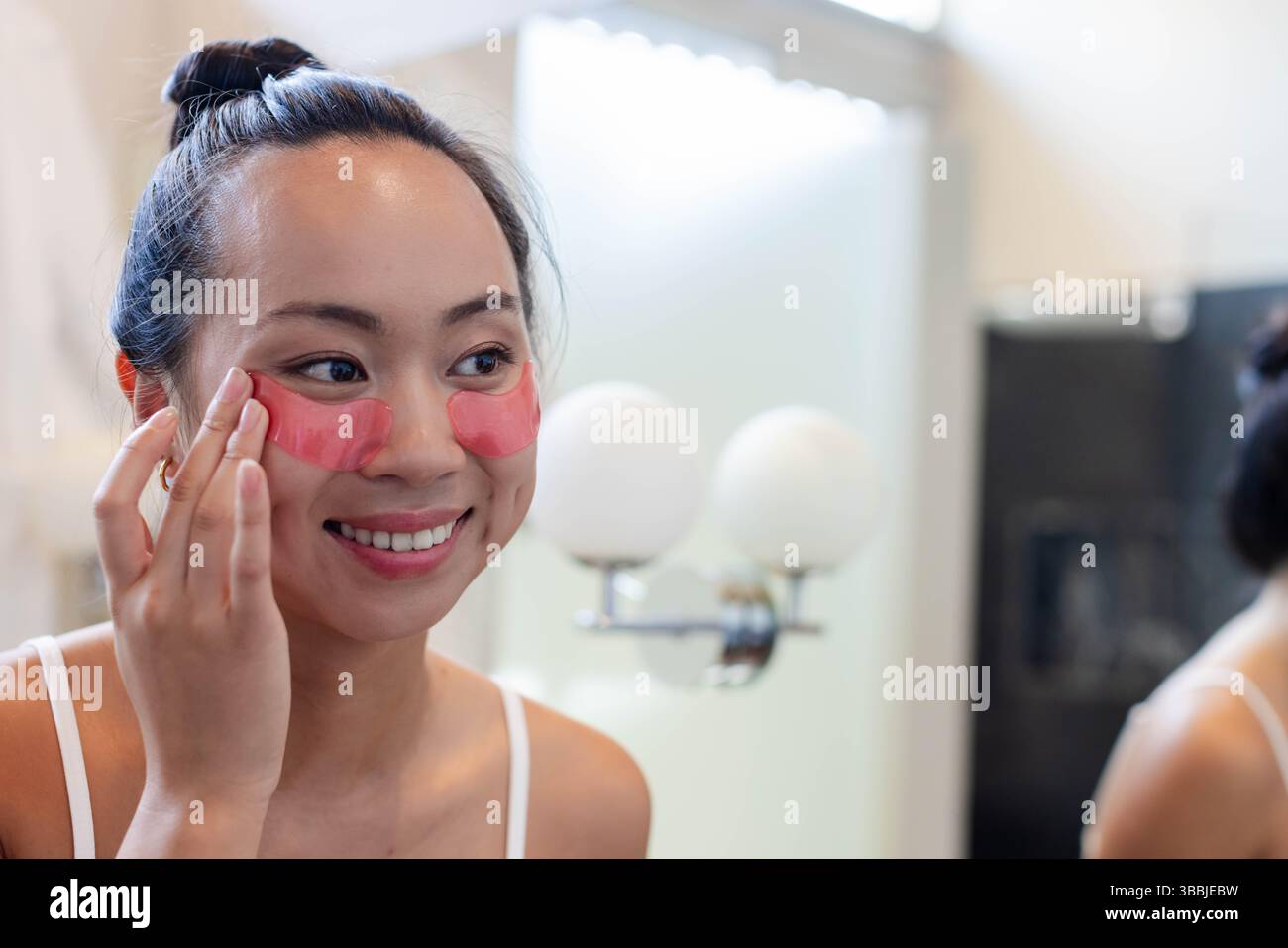 Applying hydrogel patches under eyes Chinese woman at bathroom mirror ...