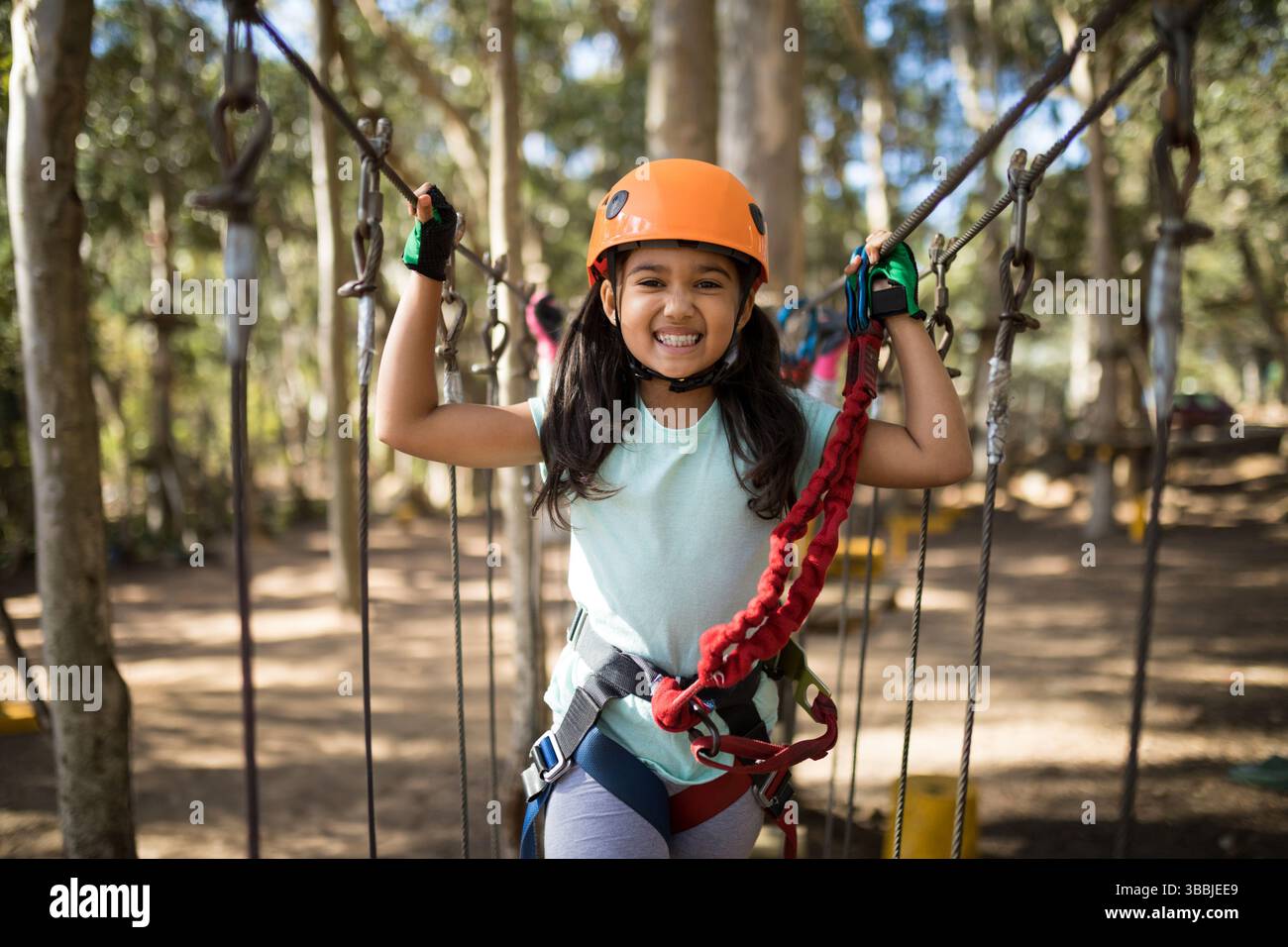 Smiling child girl balancing on rope bridge at forest ropes course ...