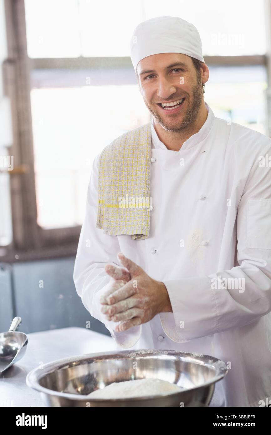 Smiling mid-adult male chef dusting with flour in commercial kitchen ...