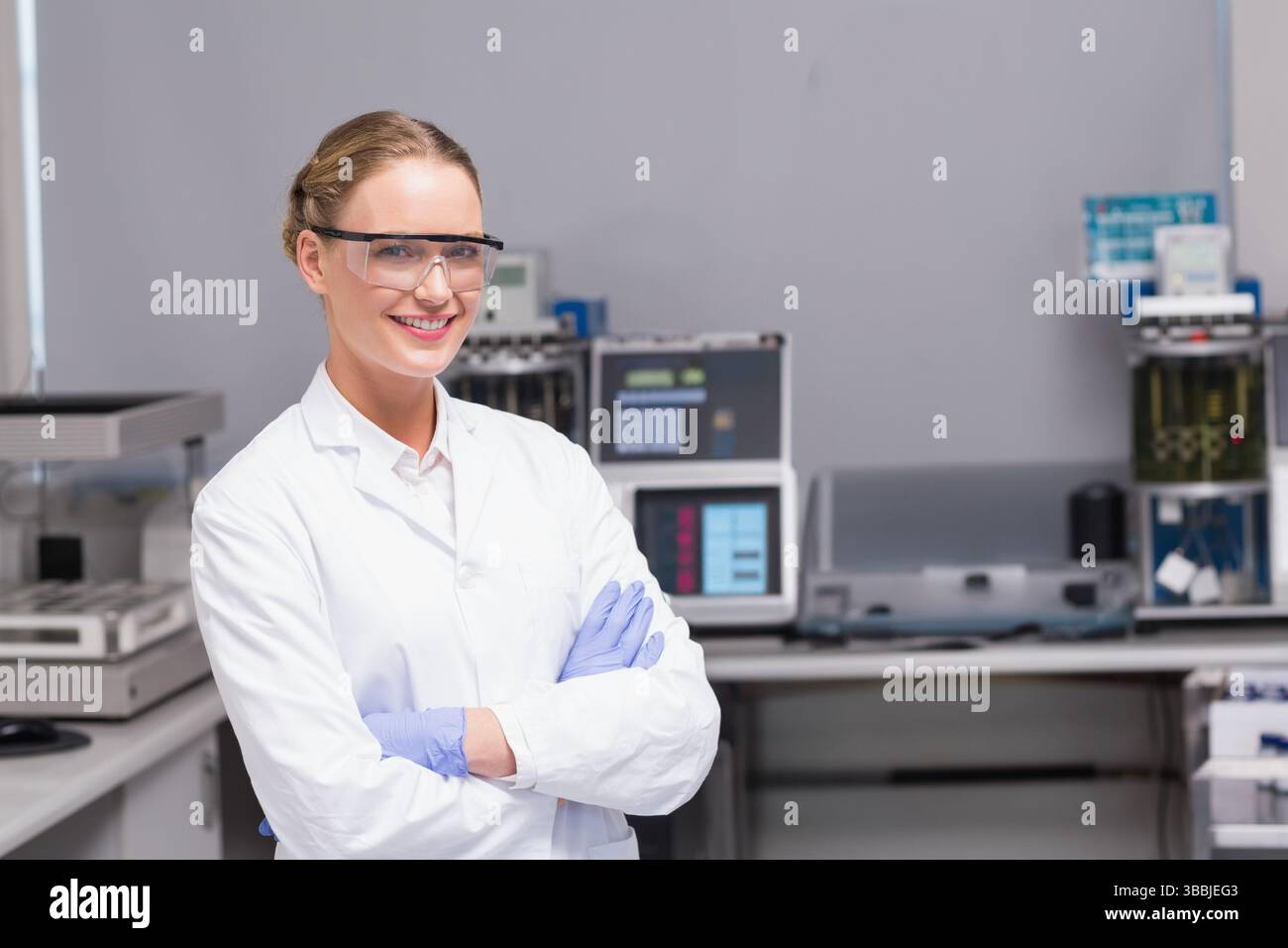 Smiling female scientist crossing arms in modern lab, with analyzers ...