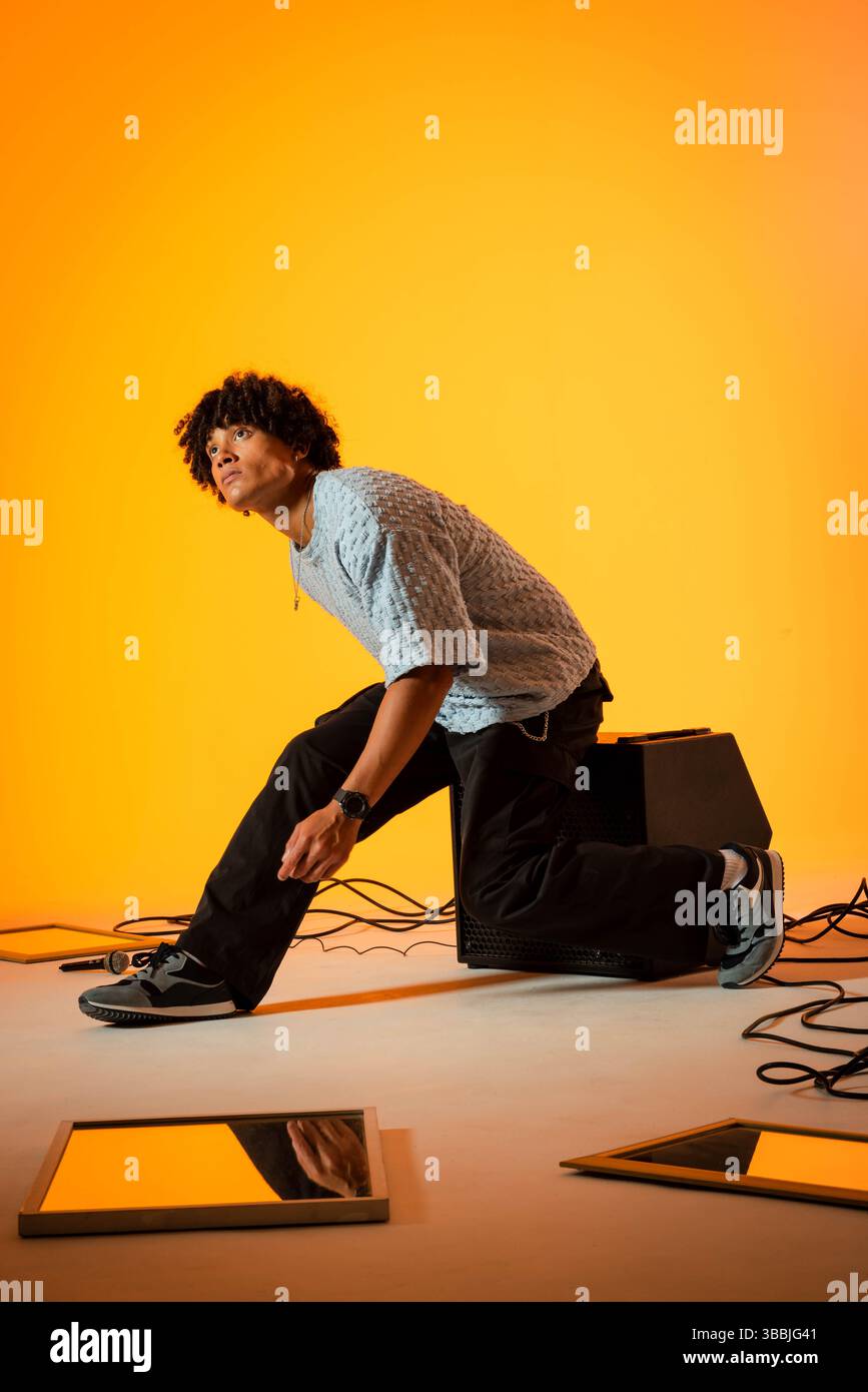 Kneeling male model leaning forward on orange backdrop, with reflective ...
