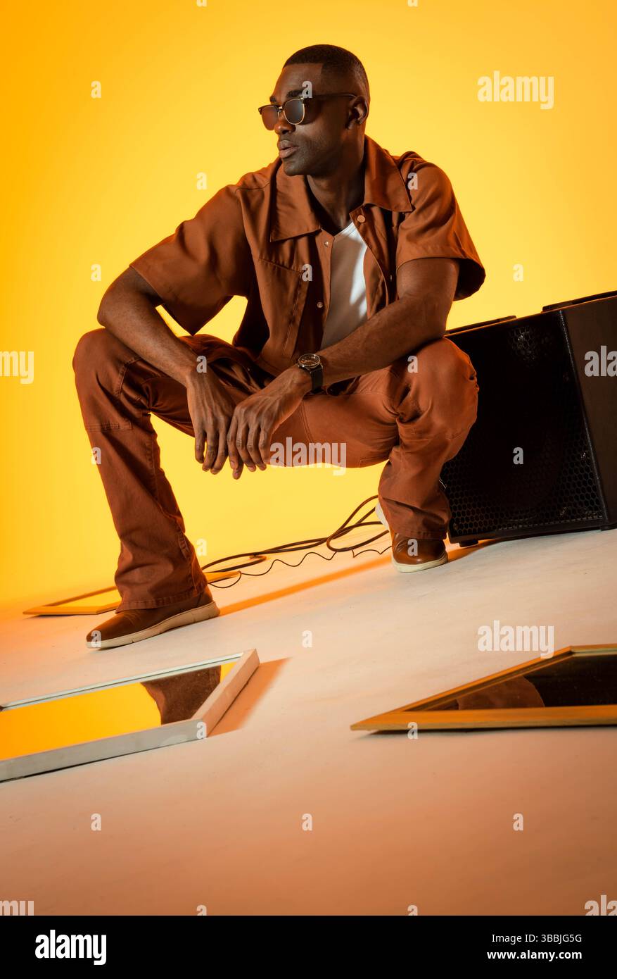 Crouching African American man wearing brown outfit in studio, with ...