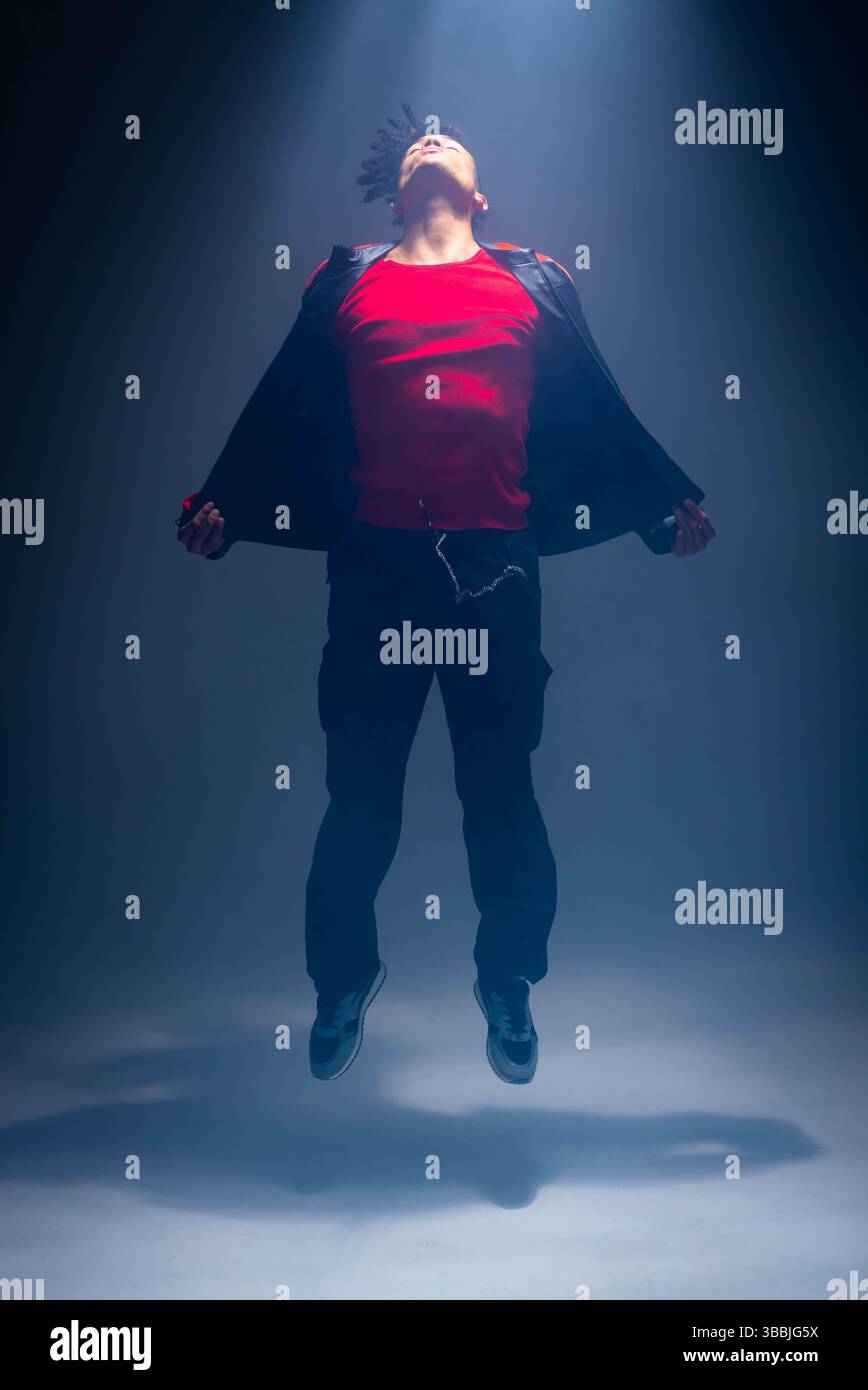 Levitating male dancer wearing red shirt and black jacket in misty ...