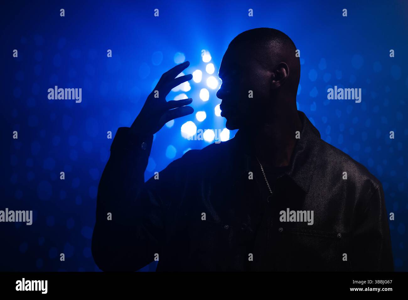 Standing African American man raising hand near face against dark stage ...