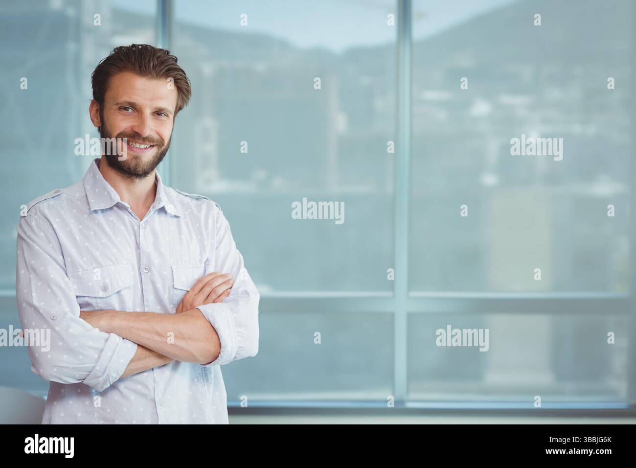 Standing man in 30s crossing arms in modern office space, with floor-to ...