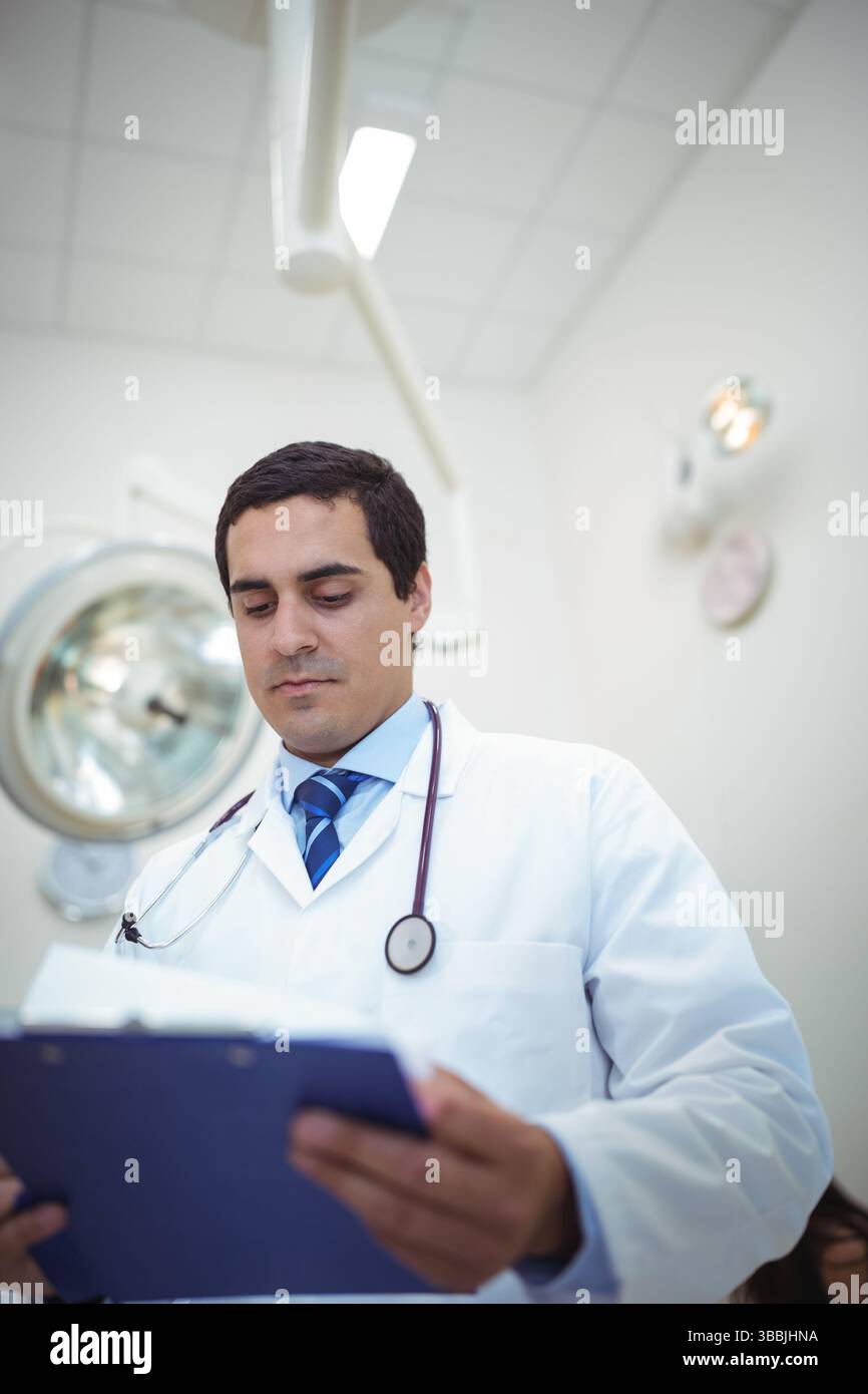 Reviewing blue clipboard male doctor wearing stethoscope in exam room ...