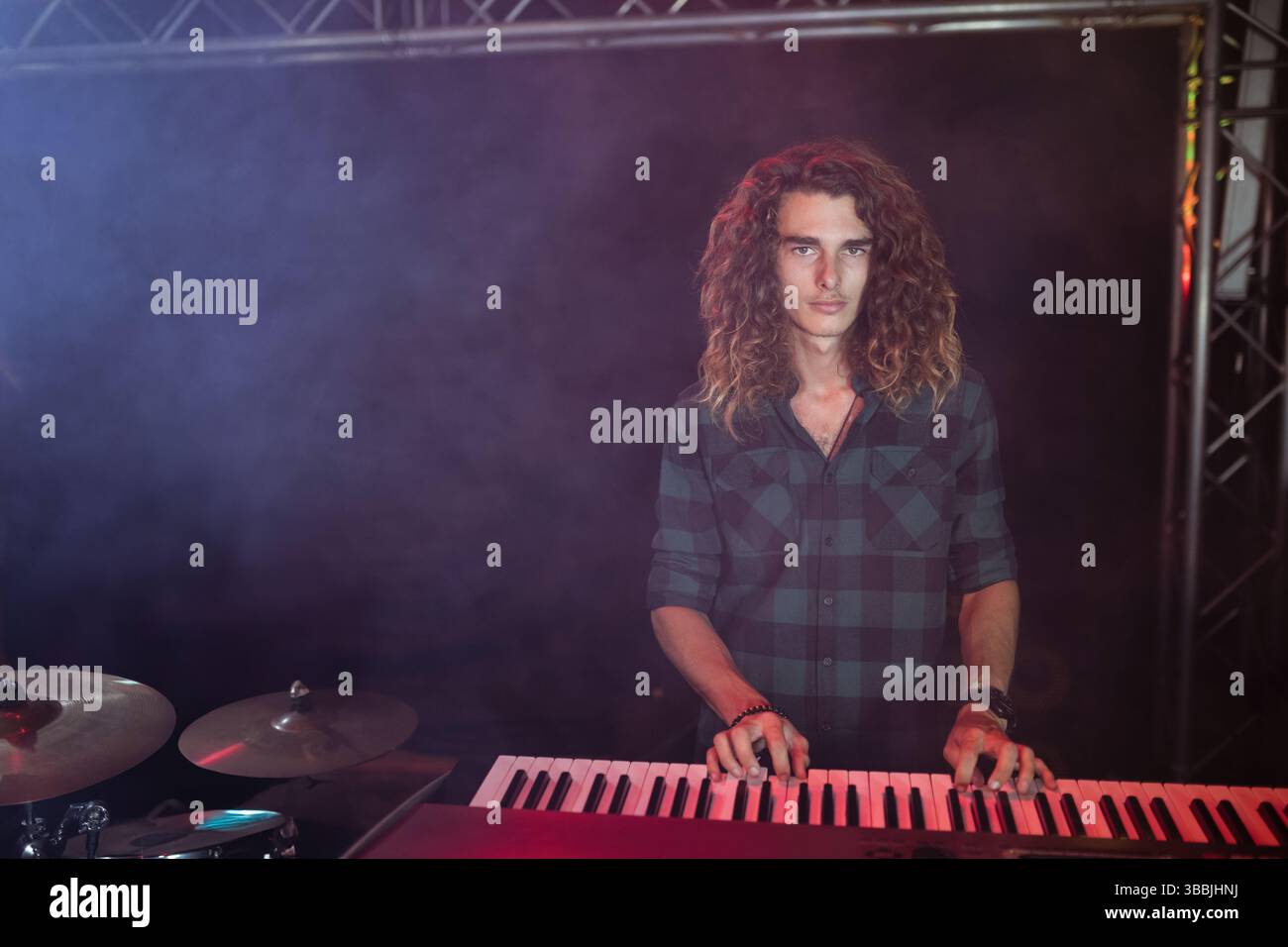 Red keyboard is resting beside drum cymbals on dark stage, illuminated ...