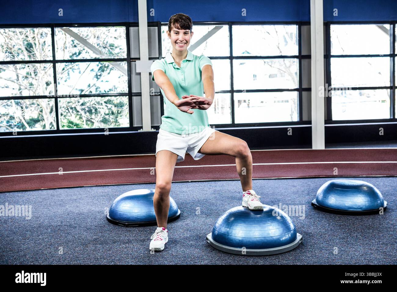 Adult woman performing squat on blue Bosu trainer in gym studio near ...
