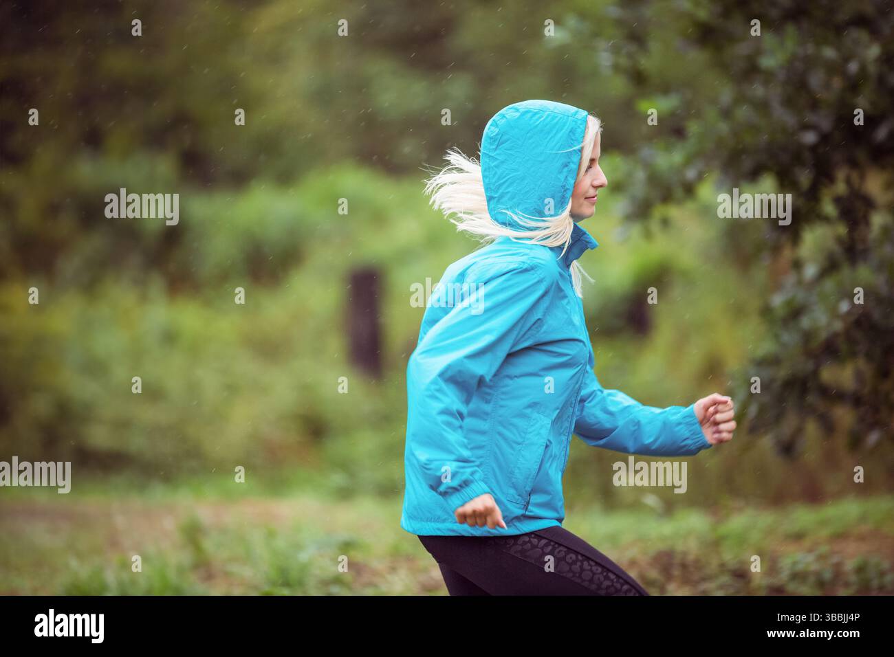 Runner is jogging on forest trail in light rain wearing blue hooded ...