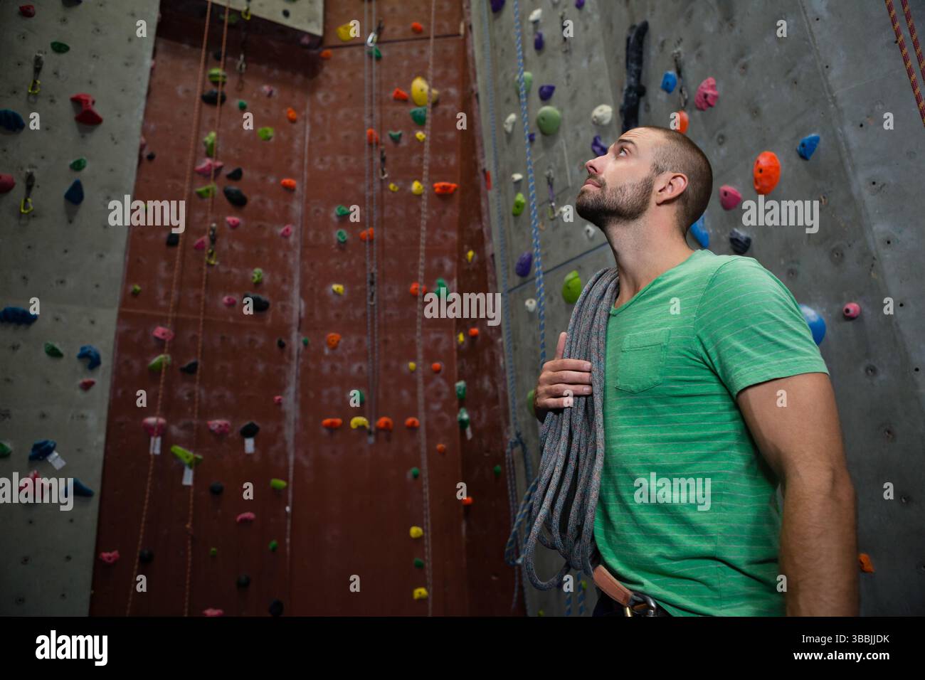 Holding coiled climbing rope over shoulder, man in late 20s surveying ...