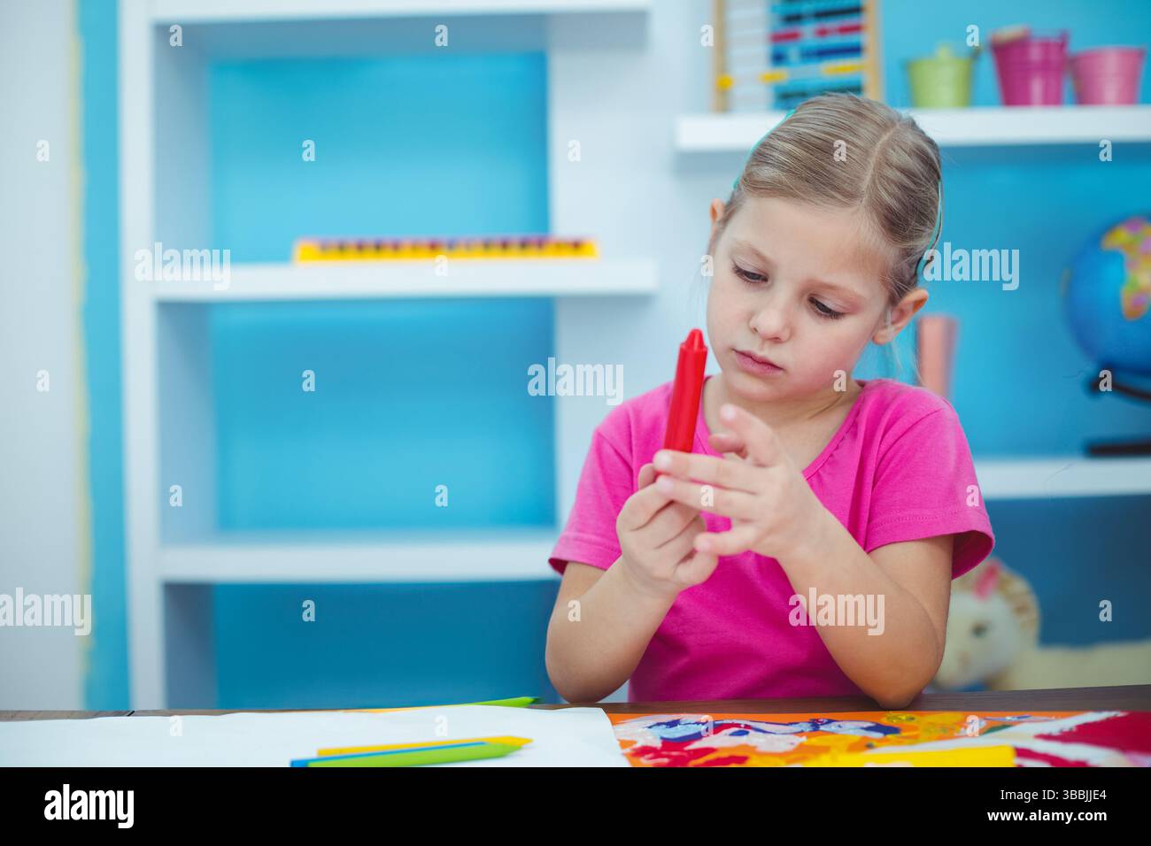 Drawing child girl using red marker in playroom, with shelving unit and ...