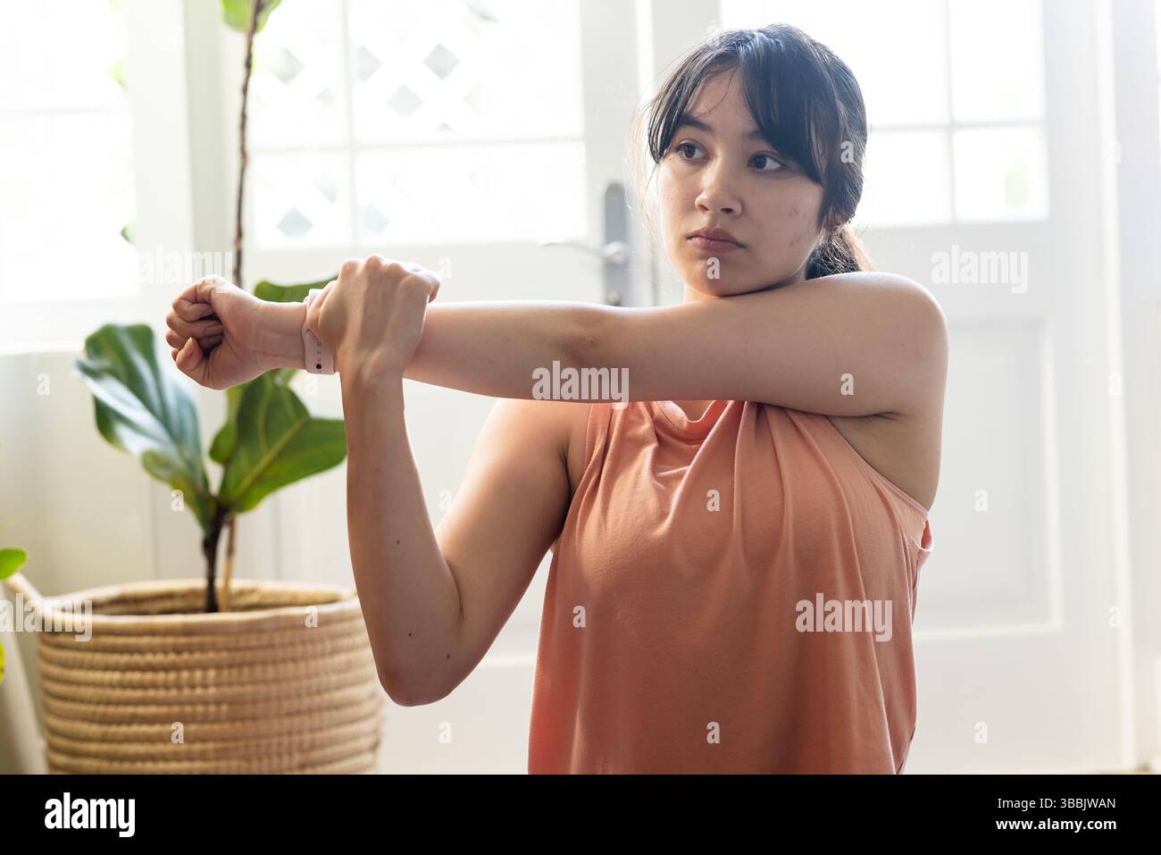Asian woman in peach workout top stretching arm across chest in ...