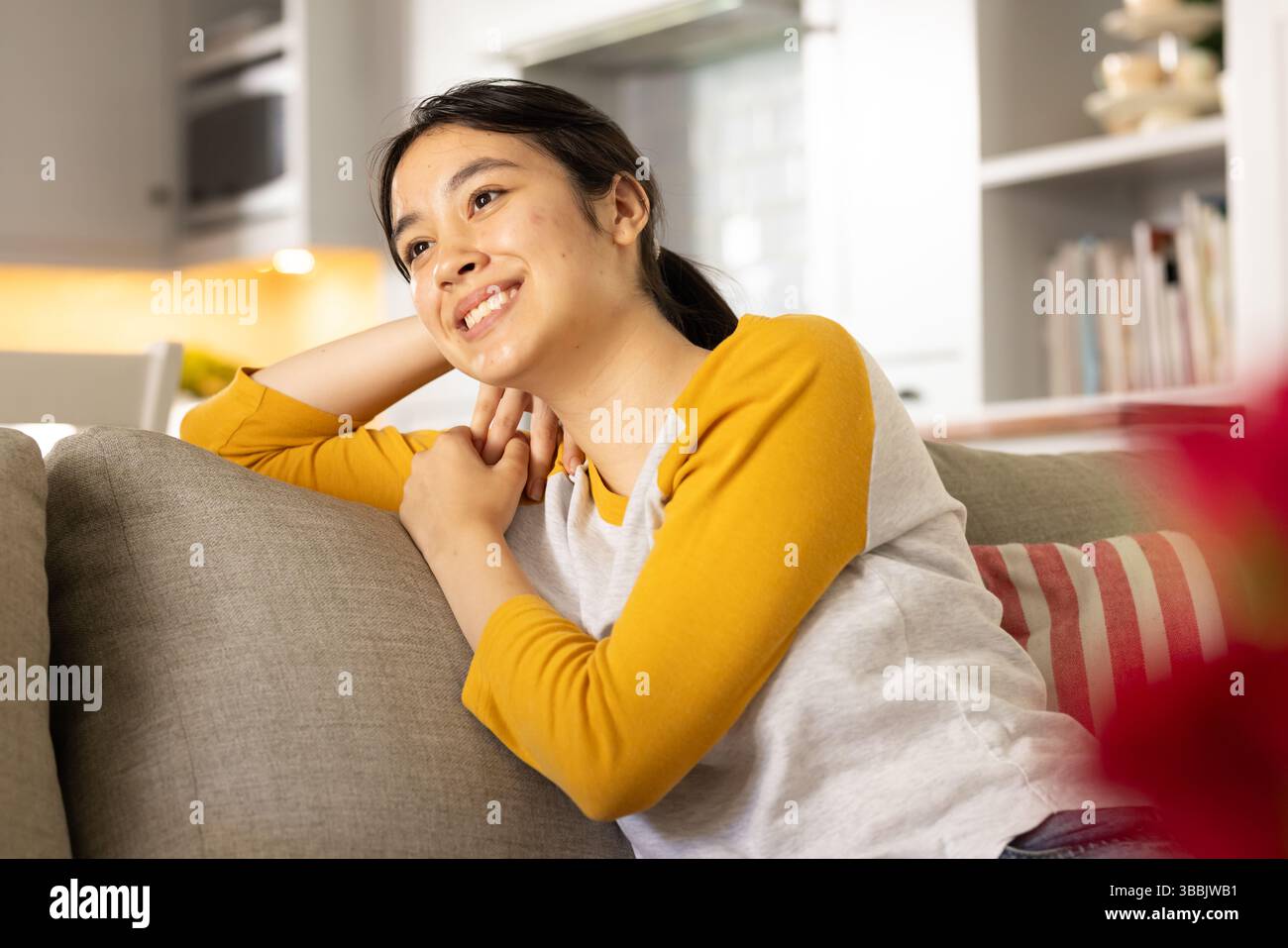 Leaning Asian woman resting head on gray sofa in living room, with red ...