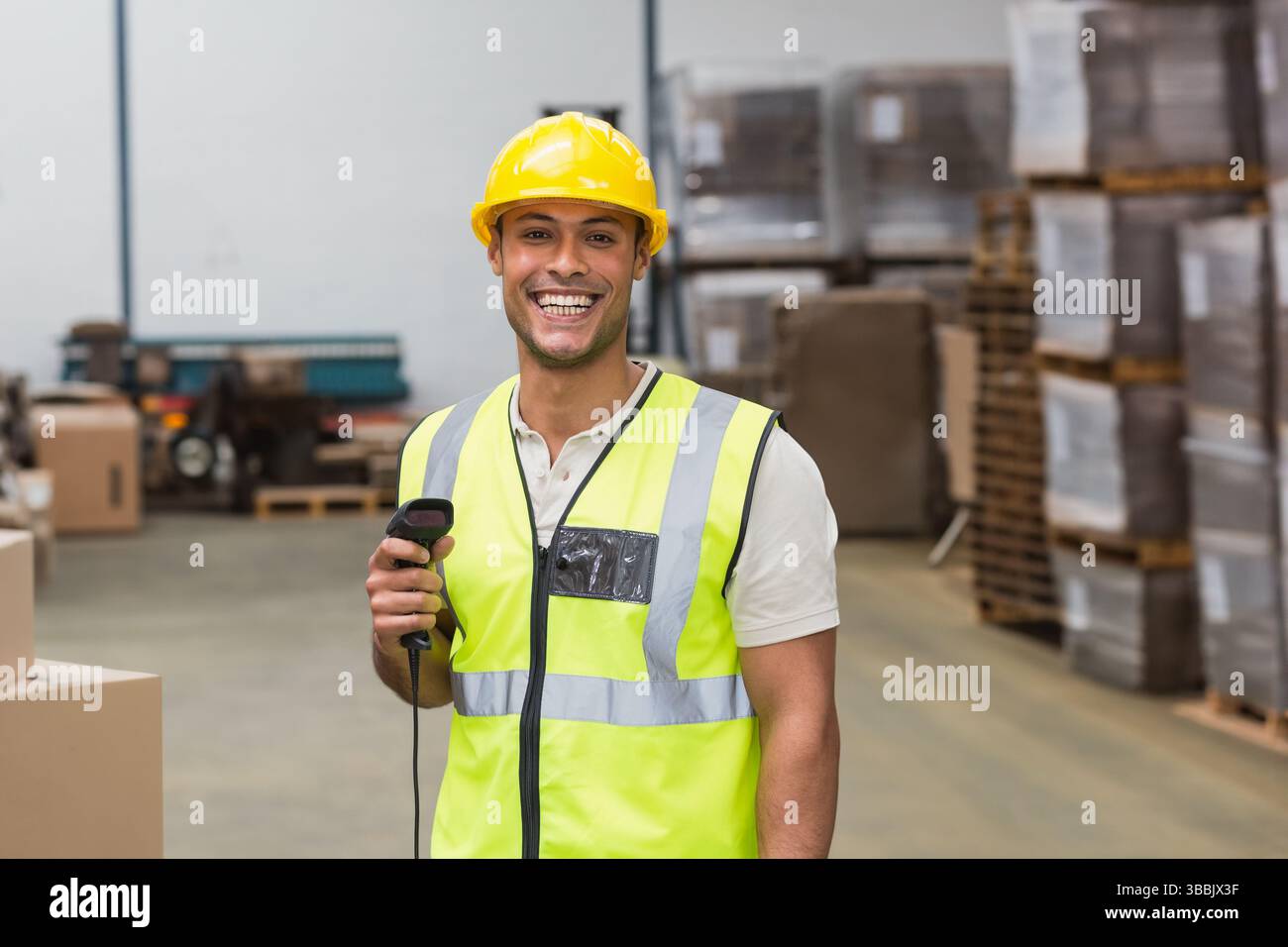 Smiling male warehouse worker holding barcode scanner in busy ...