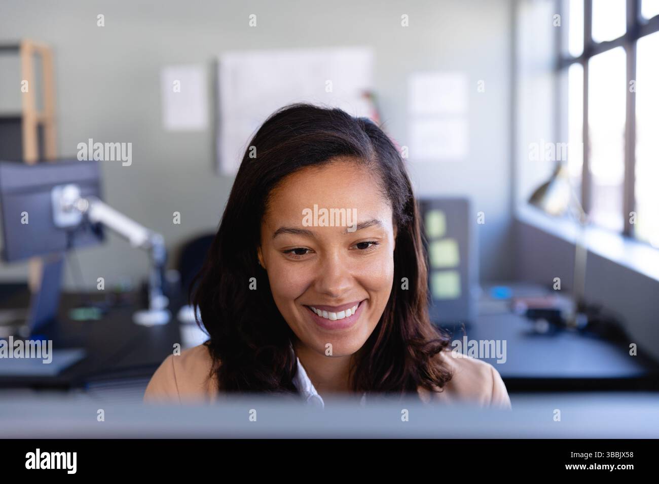 Smiling woman typing on keyboard at modern office desk with computer ...