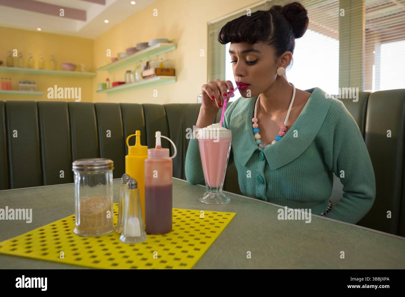 Woman sipping pink milkshake in retro diner booth with pastel walls ...