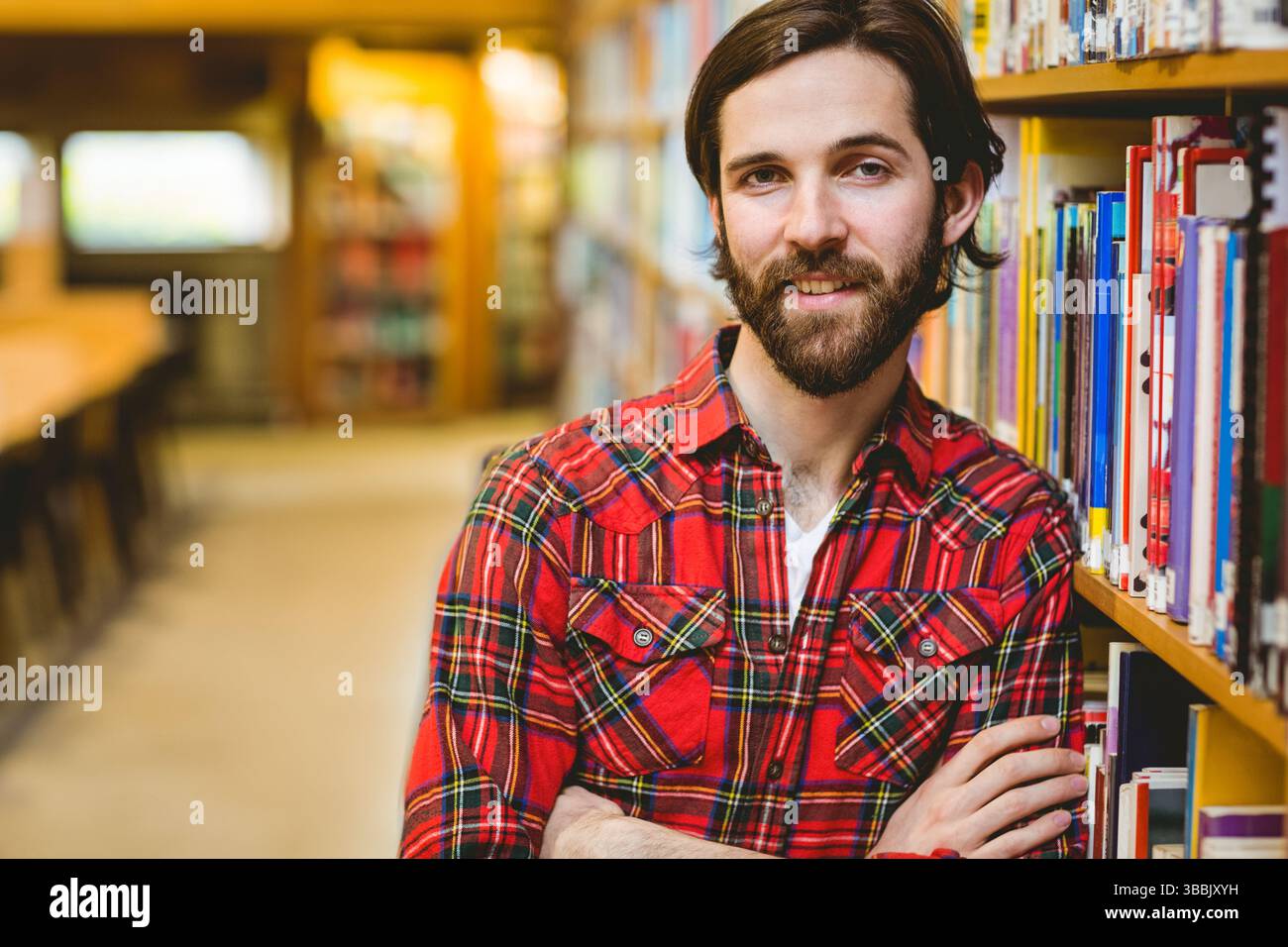 Smiling man leaning against bookshelf in library aisle, with rows of ...