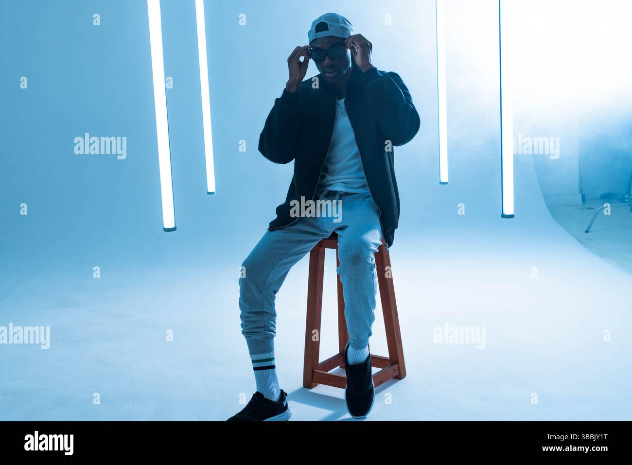 Adjusting sunglasses African American male wearing cap sitting on stool ...