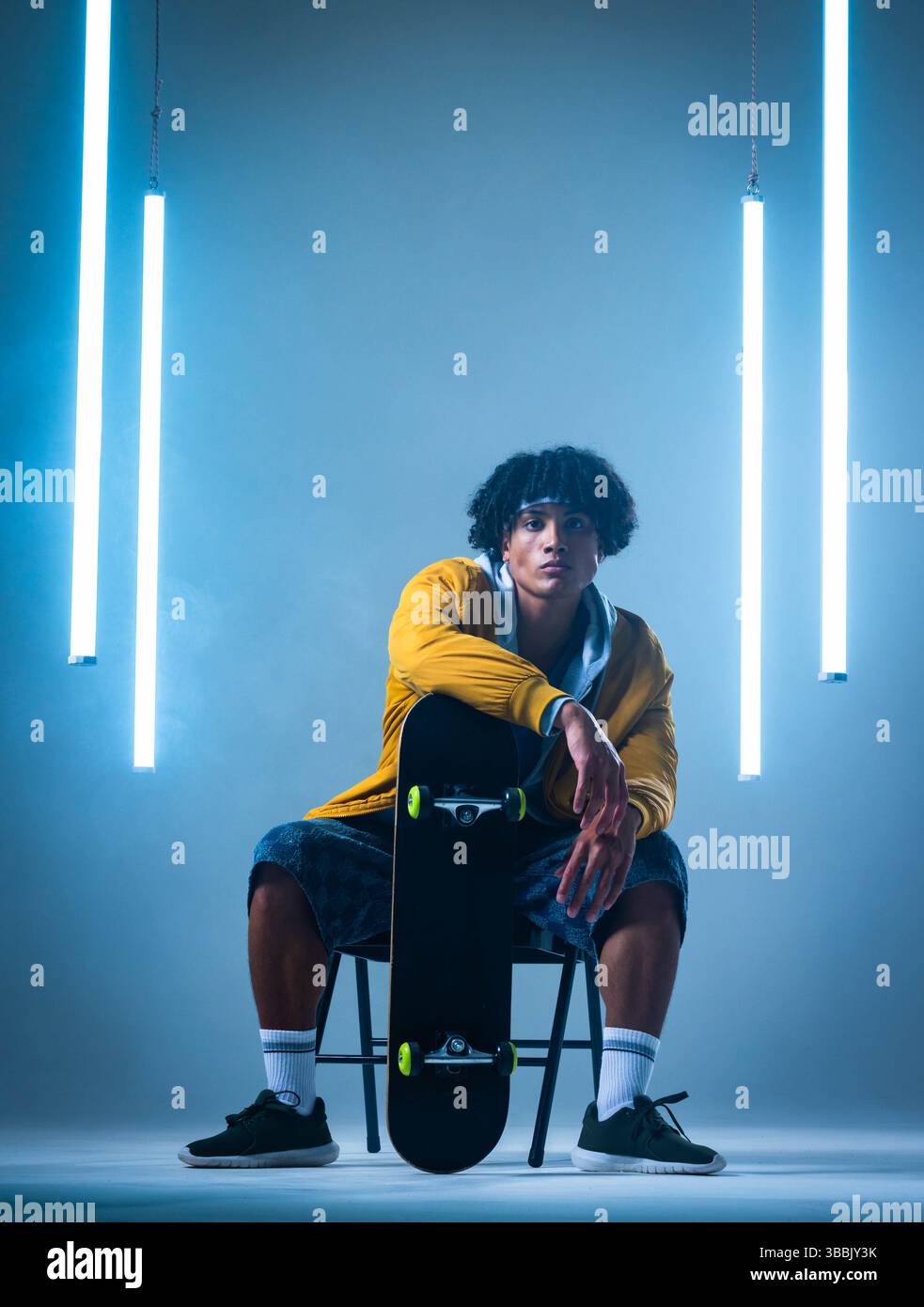 Sitting man holding skateboard vertically in photography studio, with ...
