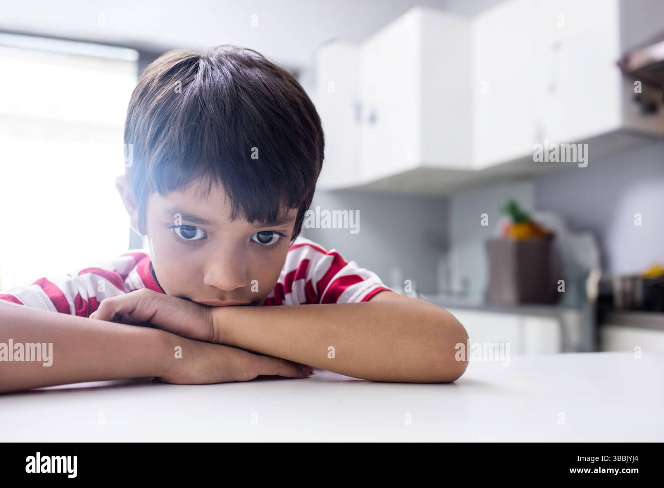 Boy is resting chin on folded arms on white kitchen counter, with fruit ...